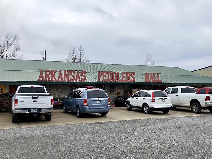 The bright red letters of Arkansas Peddlers stand like a welcoming carnival barker against the sky, with that charming green dinosaur keeping watch over vintage treasures.
