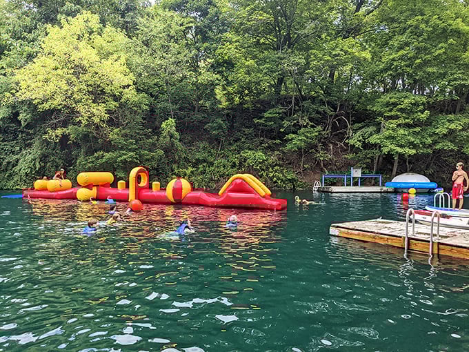 Where the magic happens! Colorful inflatable obstacles float invitingly on crystal-clear quarry waters, promising adventures that'll make your inner child high-five your actual children.