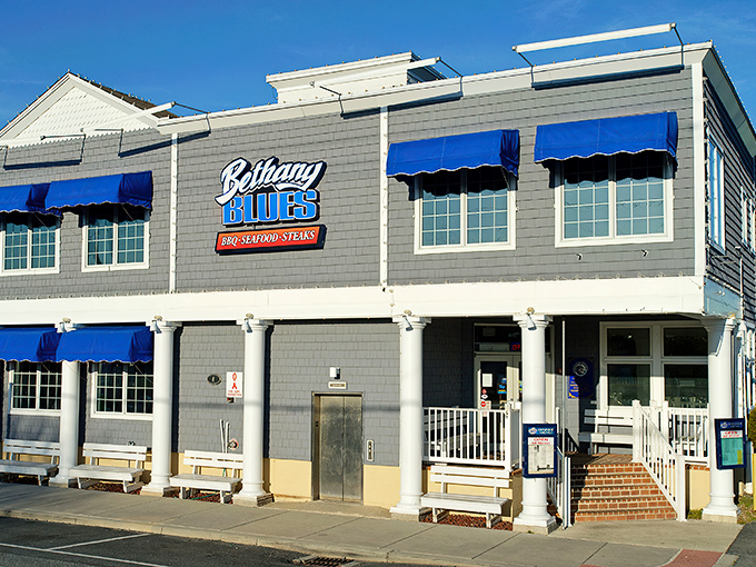 The coastal charm of Bethany Blues' exterior, with its distinctive blue awnings and gray shingles, beckons hungry travelers like a barbecue lighthouse on Delaware's shore.