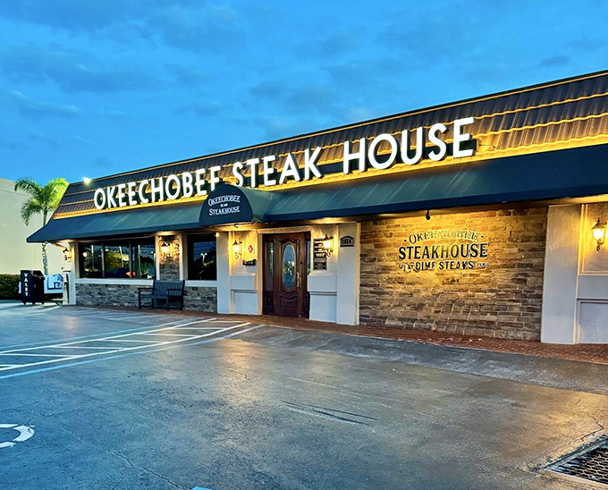 The blue awning of Okeechobee Steakhouse glows like a beacon at dusk, promising carnivorous delights within this Palm Beach institution since 1947.