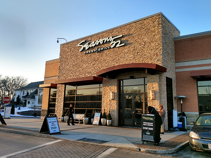 The stone facade of Seasons 52 stands like a culinary lighthouse, beckoning hungry travelers with its warm glow and those unmistakable bright green umbrellas.