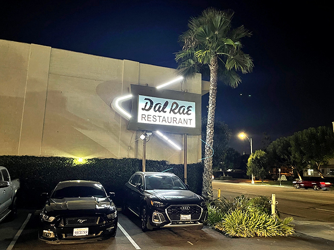 The neon sign beckons like a lighthouse for hungry souls. Palm trees and classic cars complete this quintessential Southern California supper club scene.