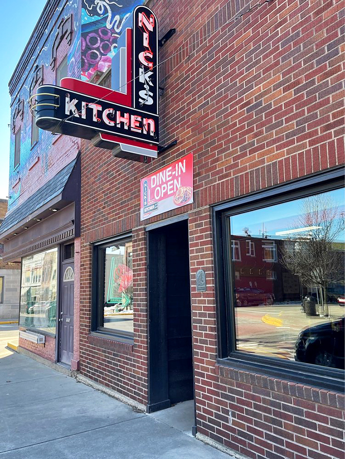 The iconic red neon sign of Nick's Kitchen stands as a beacon of breakfast hope against the brick facade, promising culinary treasures within.