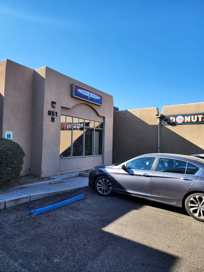 The unassuming adobe exterior of Whoo's Donuts, where Santa Fe's sweetest treasures await behind that neon "OPEN" sign. Donut paradise incognito!