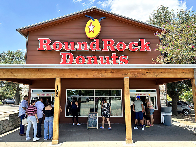 The iconic wooden and limestone facade of Round Rock Donuts stands proudly under Texas skies, beckoning donut pilgrims with its famous red signage.