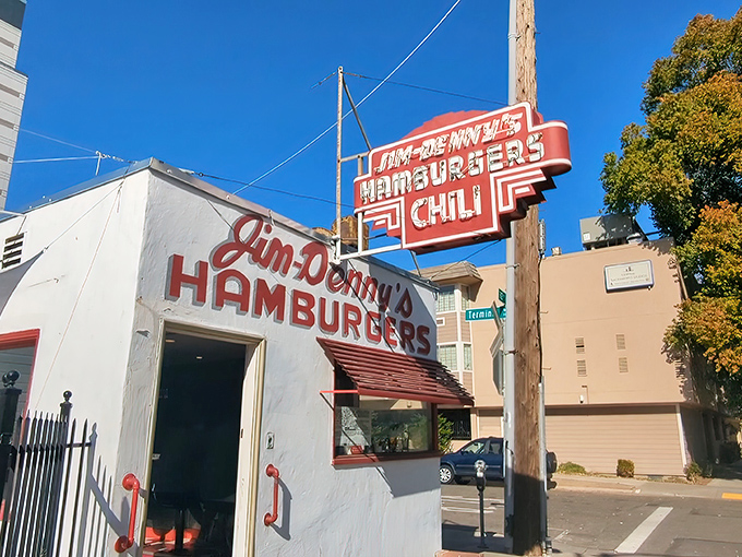 That iconic red sign against the blue California sky is like a beacon for burger lovers. Jim-Denny's modest exterior hides culinary greatness within.