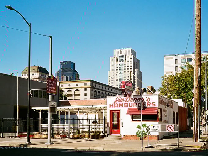 That iconic red sign against the blue California sky is like a beacon for burger lovers. Jim-Denny's modest exterior hides culinary greatness within.