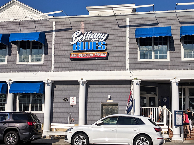 The coastal charm of Bethany Blues' exterior, with its distinctive blue awnings and gray shingles, beckons hungry travelers like a barbecue lighthouse on Delaware's shore.