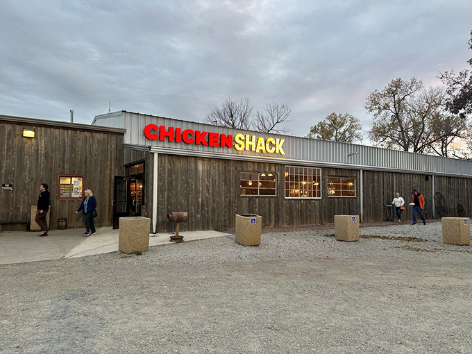 The humble wooden exterior of Chicken Shack stands proudly against an Oklahoma sky, its bold red and yellow sign promising poultry perfection inside.