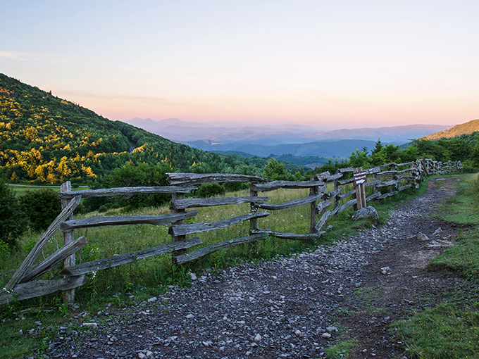Sunset paints the Blue Ridge Mountains in watercolor hues while a rustic fence guides your journey. Nature's version of the yellow brick road.
