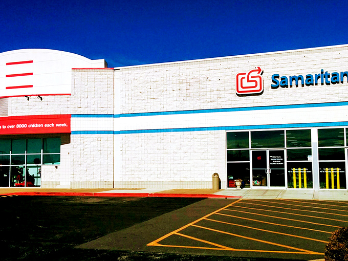 The exterior of Samaritan Shop stretches wide like a treasure chest waiting to be opened, its blue banner promising adventures in second-hand splendor.