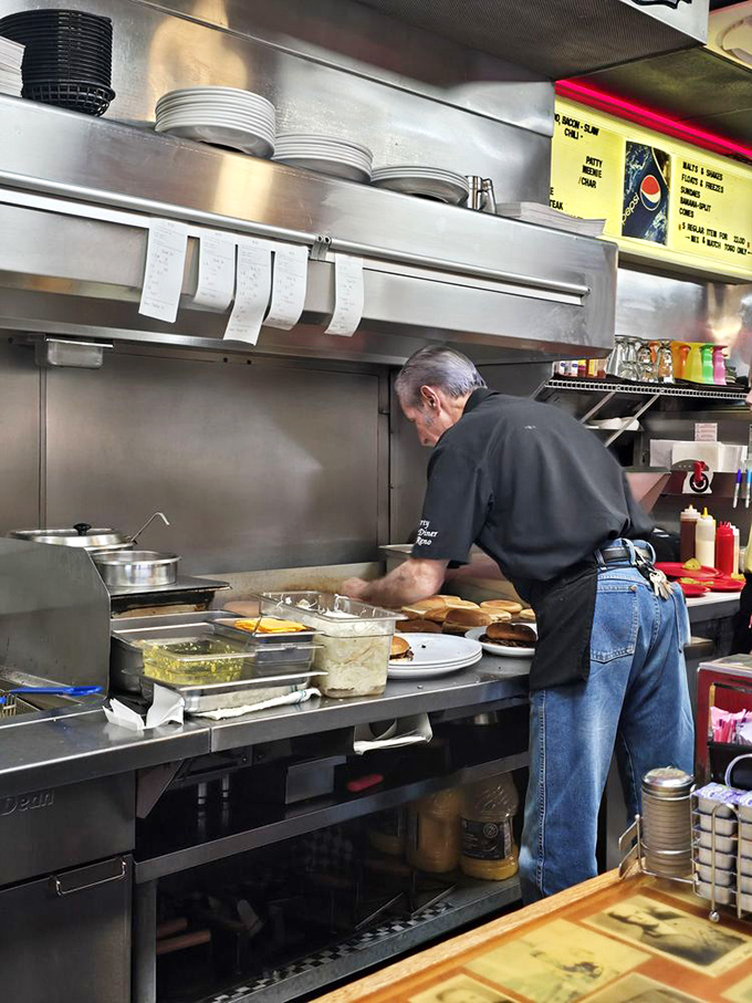 Culinary choreography happens behind this counter, where experienced hands have pressed thousands of onions into countless patties with practiced precision.