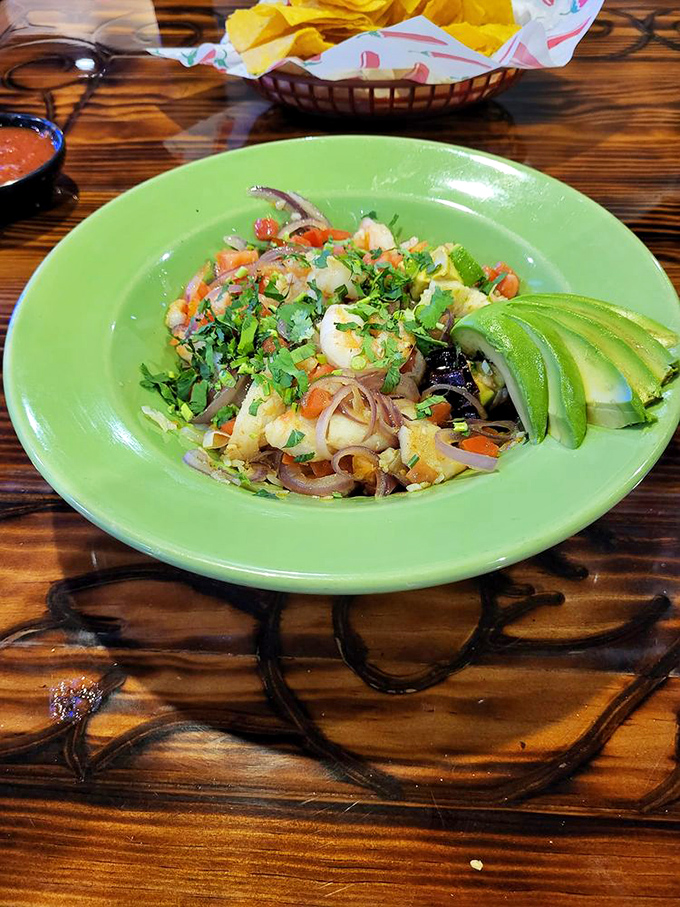 Seafood that dances with cilantro and fresh vegetables, staged on a vibrant green plate. Avocado slices stand by as willing accomplices.