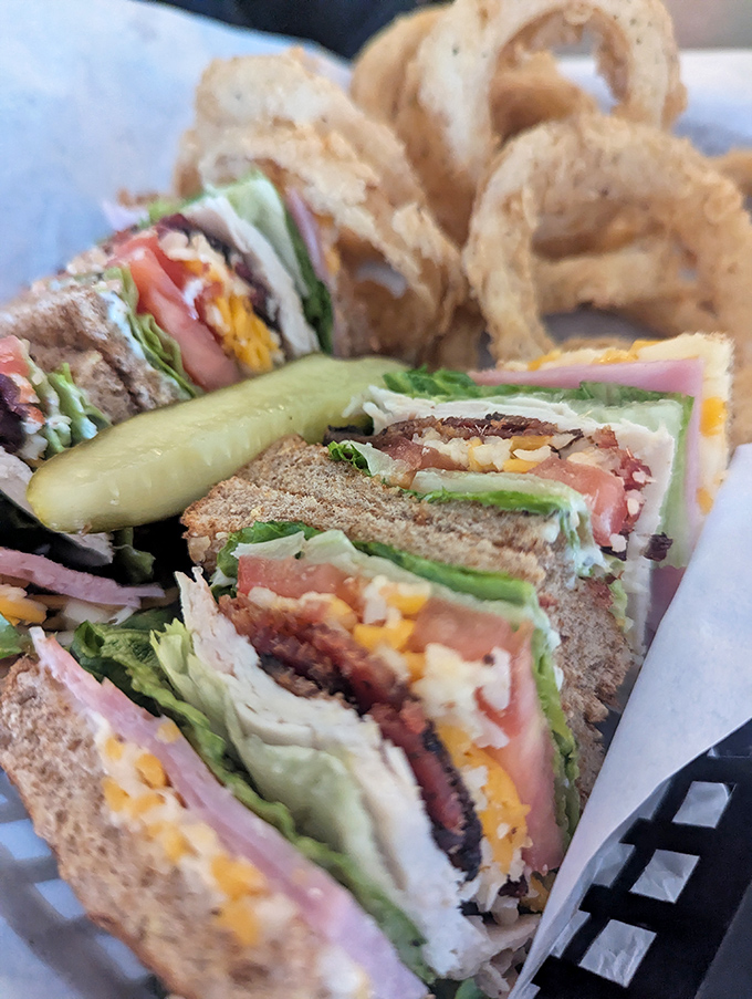 A club sandwich stacked higher than your weekend plans, with layers that tell a delicious story. Those onion rings are the perfect punctuation.