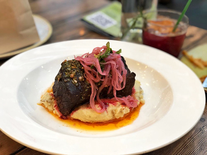A short rib so tender it practically surrenders to your fork, resting on a cloud of mashed potatoes with pickled onions for contrast.
