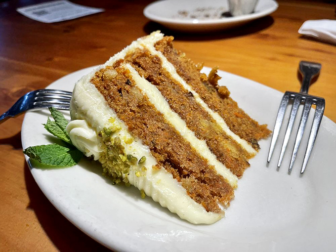 A slice of carrot cake tall enough to require FAA clearance, with cream cheese frosting that demands a moment of silent appreciation.