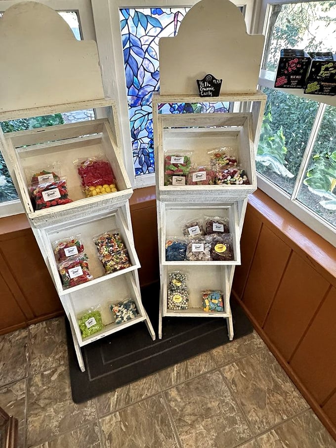 White display stands creating a candy altar by the window. The sunlight streaming through stained glass transforms ordinary sweets into stained glass themselves.