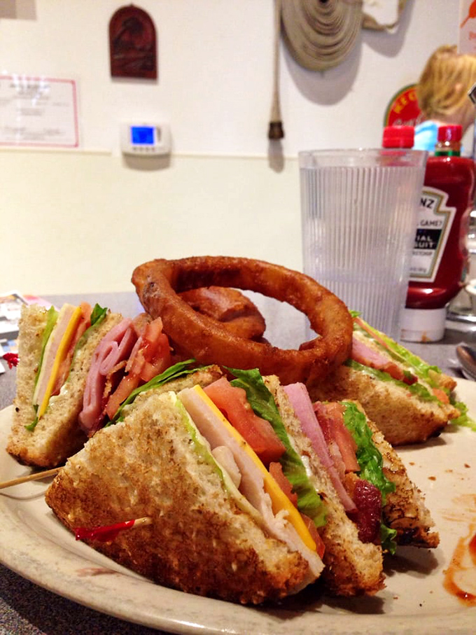 A club sandwich that towers with ambition, accompanied by an onion ring that deserves its own fan club.