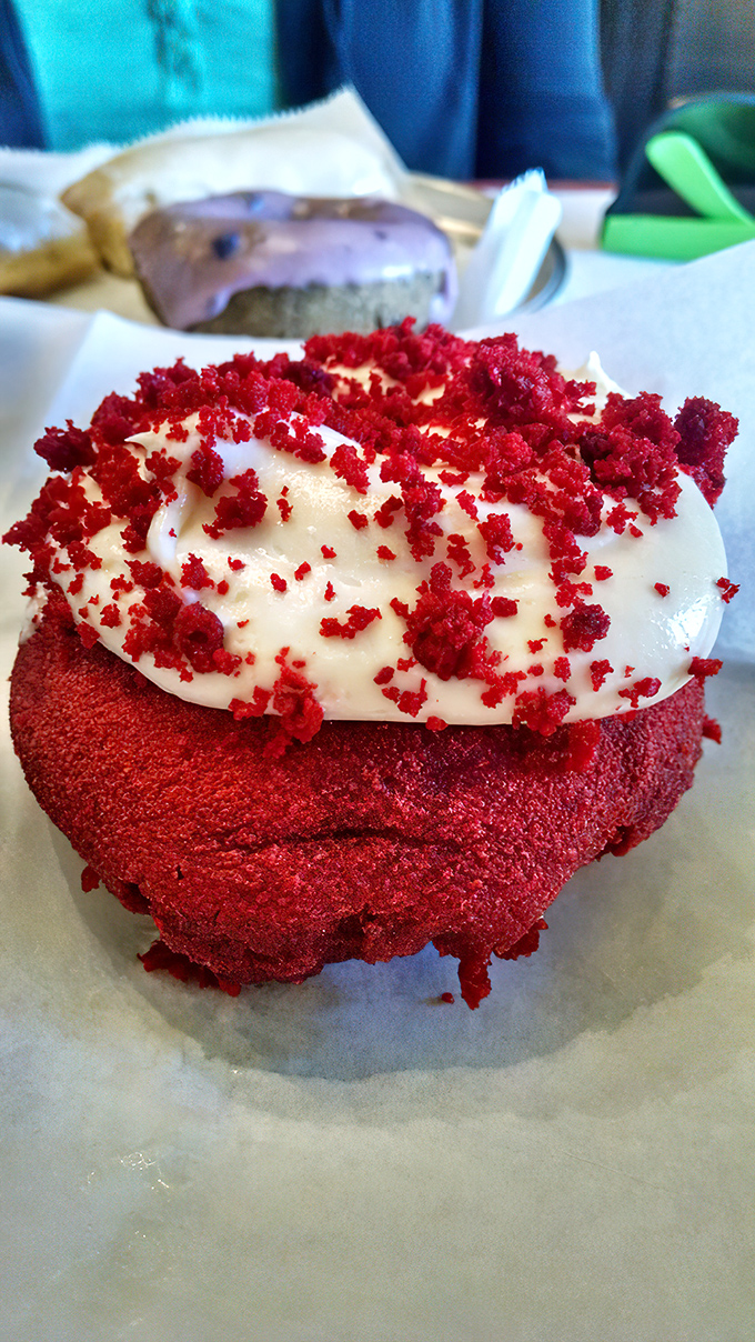 The red velvet donut wears its cream cheese frosting like formal attire, dressed up for a black-tie affair in your mouth.