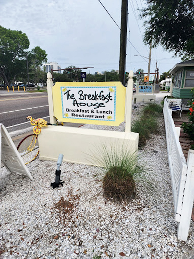 The roadside sign stands like a humble ambassador, giving no hint of the breakfast wonderland that awaits beyond the white fence.