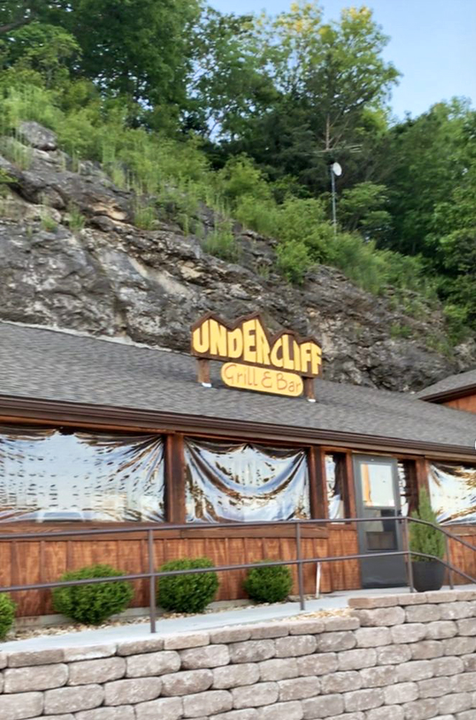 The sign says it all&mdash;you're literally dining under a cliff. Yellow letters pop against ancient stone in a visual promise of adventure.