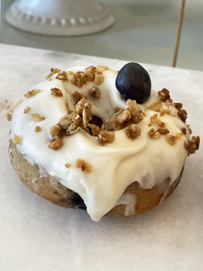 Crowned with crunchy walnuts and a single blueberry sentinel, this cream-topped creation bridges the gap between donut and sophisticated dessert.