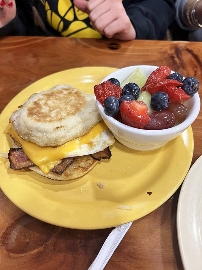 Breakfast sandwich perfection: English muffin, melty cheese, bacon, and egg, with fresh fruit that makes you feel virtuous despite your indulgence.