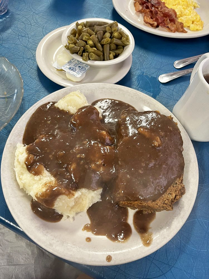 Meatloaf swimming in gravy lake with mashed potato islands&mdash;comfort food cartography at its most delicious.