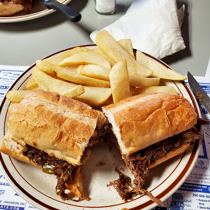 A pulled pork sandwich cut in half reveals its tender secrets. Those steak fries look like they mean business.