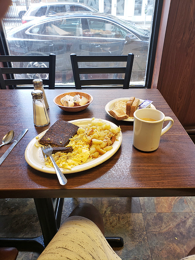 The classic American breakfast tableau: eggs, scrapple, home fries, toast, and a mug of coffee that promises to understand your morning struggles.