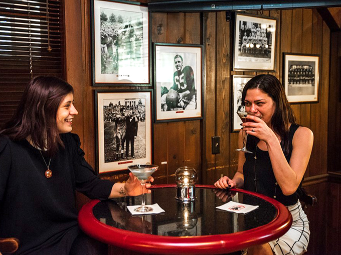 Two friends sharing cocktails and conversation against a backdrop of vintage sports memorabilia&mdash;proof that some traditions never need updating.