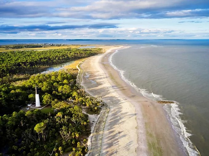 Hunting Island's lighthouse stands sentinel over pristine shoreline, a white exclamation point against South Carolina's curved coastline and verdant forest.
