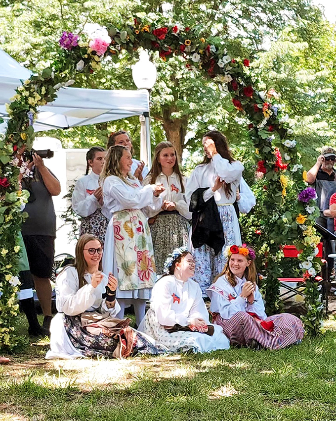 During Midsummer Festival, young women in traditional dress celebrate under flower arches, continuing centuries-old Swedish traditions under Kansas skies.