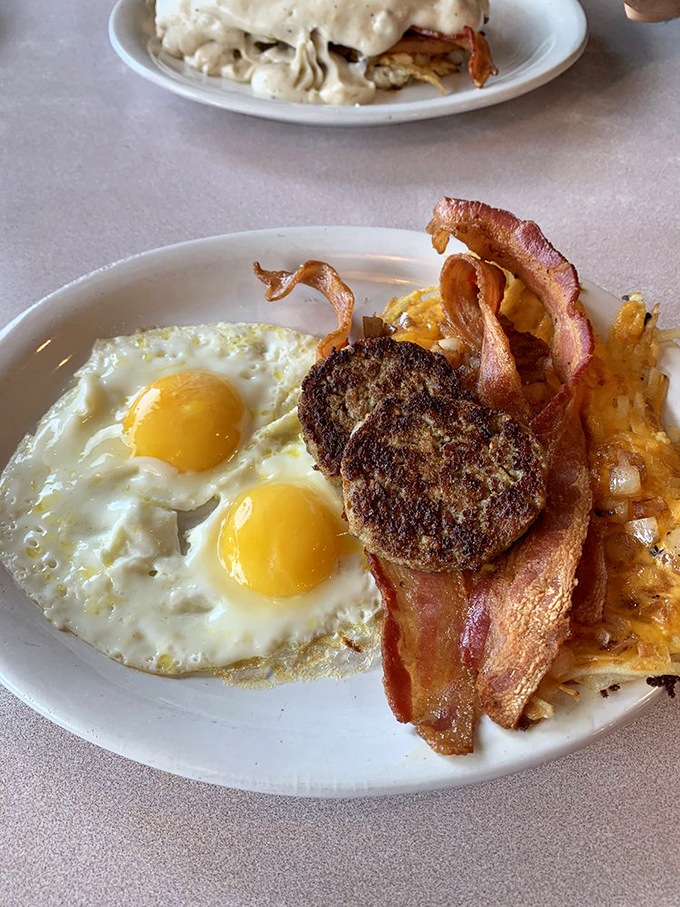 Two sunny-side-up eggs staring back at you like optimistic eyes, with sausage patties and hashbrowns playing the perfect supporting cast.