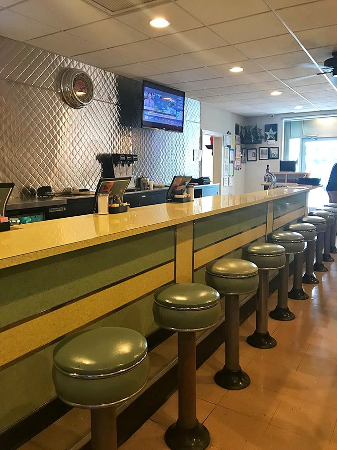 The counter where regulars claim their territory, green vinyl stools witnessing decades of conversations, confessions, and celebrations over comfort food classics.