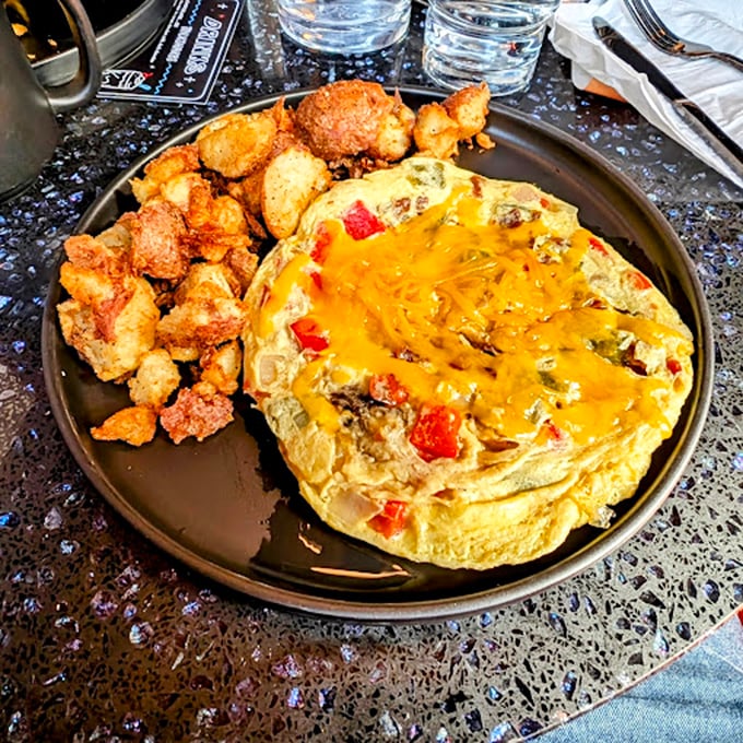 An omelet that's seen things, loaded with veggies and cheese, sitting beside potatoes that have clearly been introduced to butter and aren't looking back. 