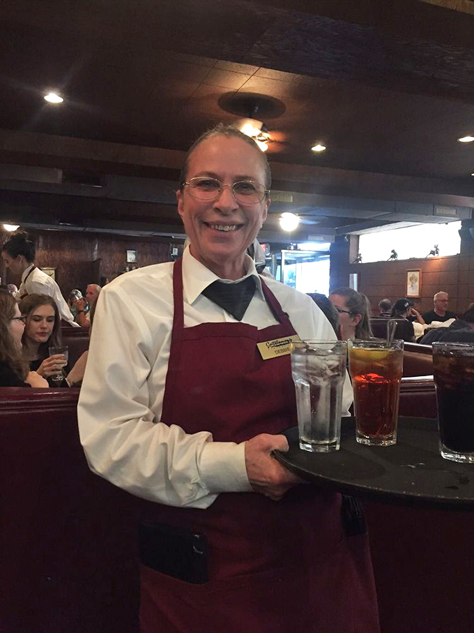 A server carrying drinks with the confidence of someone who's memorized more orders than most of us have had hot meals. The burgundy apron is practically a superhero cape.