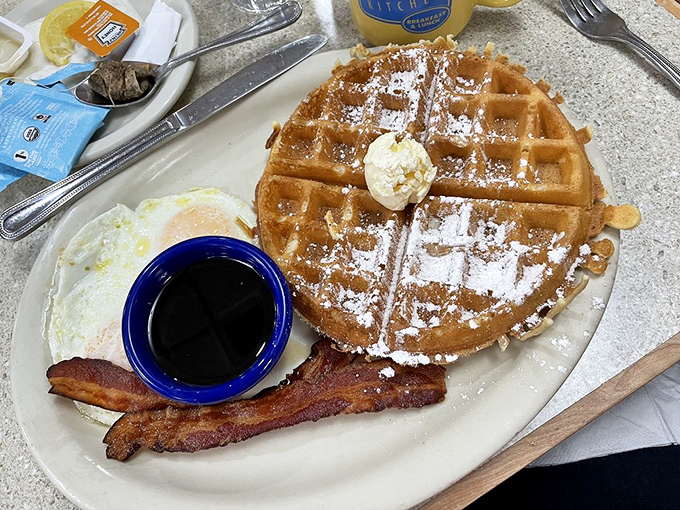 A waffle wearing powdered sugar like a winter coat, with syrup waiting in the wings to transform breakfast into an event worth waking up for.