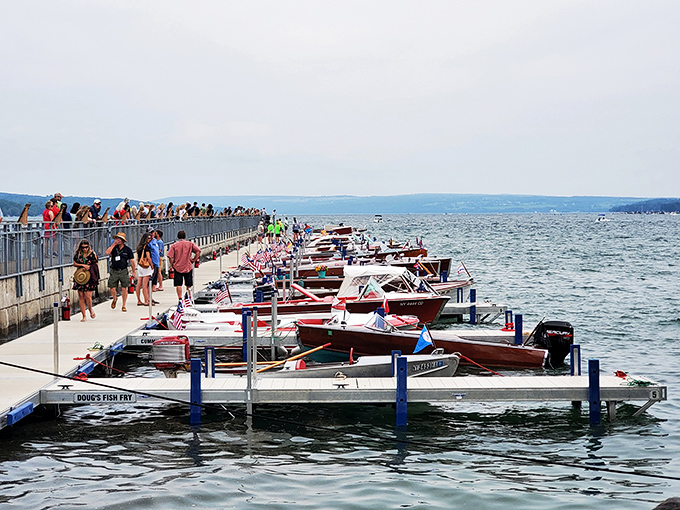 Boat enthusiasts gather along the pier during what appears to be a summer celebration. Where nautical dreams and lake life converge in colorful formation.