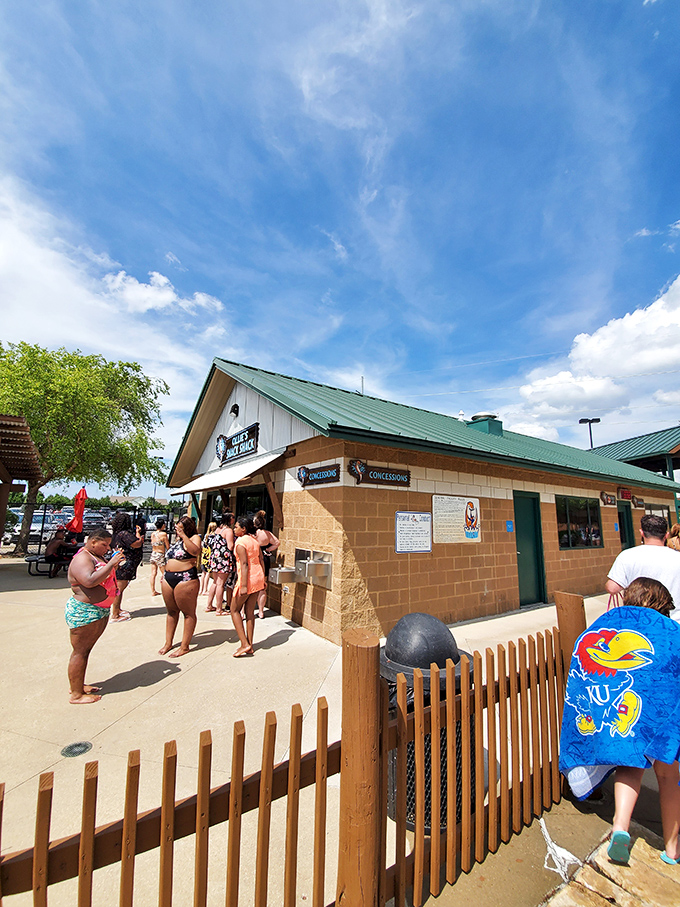 The concession stand—where chlorine-scented kids transform into negotiation experts trying to maximize their snack potential between splashes.