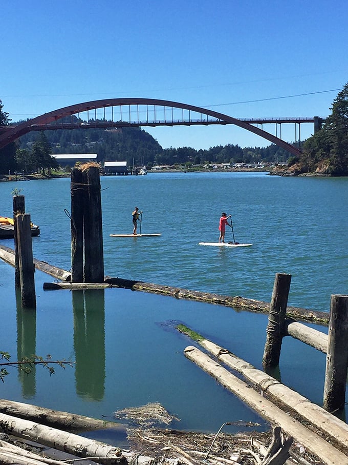 Paddleboarders glide beneath the Rainbow Bridge, balancing on water while the rest of us can barely balance our checkbooks.