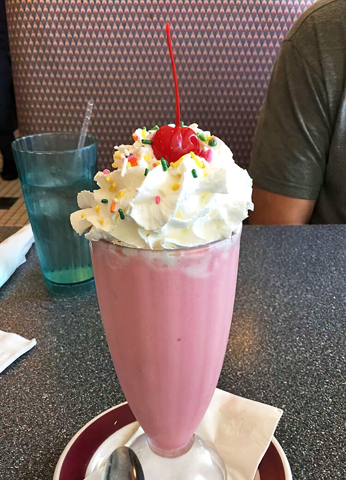 This strawberry shake isn't just a beverage, it's a dessert skyscraper with a cherry penthouse and whipped cream clouds.