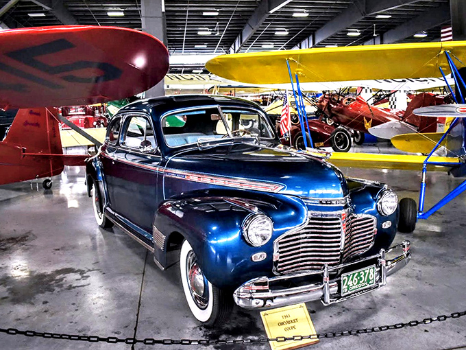 Parked beneath vintage aircraft wings, this maroon beauty reminds us when transportation was about the journey, not just the destination. 