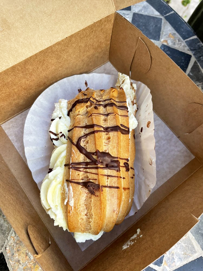 This &eacute;clair isn't just a pastry&mdash;it's a chocolate-drizzled delivery system for pure joy, nestled in its takeout container like a precious artifact.