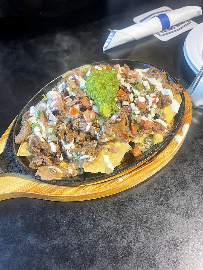 Loaded nachos arriving on their sizzling skillet &ndash; a masterclass in proper cheese-to-chip ratio that demands to be shared.