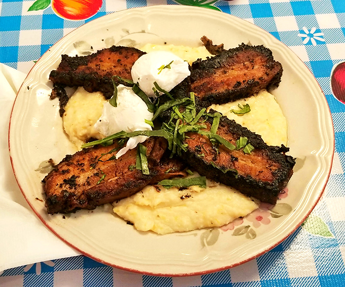 These blackened pork belly strips lounging on creamy grits are having a more relaxing morning than most of us, garnished with a poached egg that's living its best life.