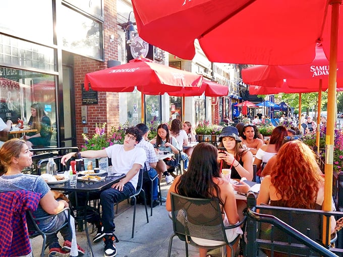 The sidewalk patio—where summer afternoons transform into evening feasts under cheerful red umbrellas in urban bliss.
