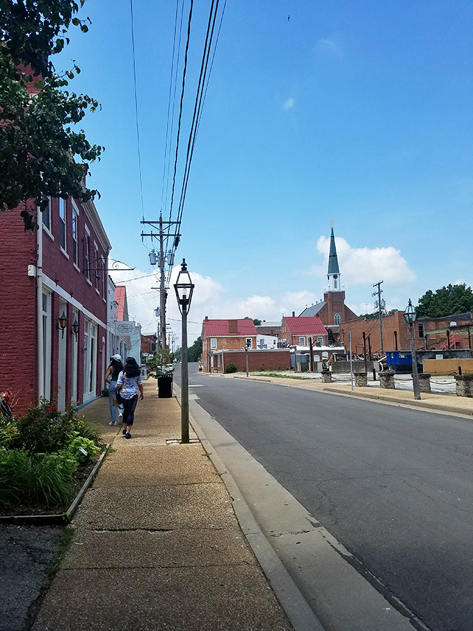 Gas lamps line pristine sidewalks where visitors stroll past carefully preserved storefronts, with the church steeple keeping watch over it all.