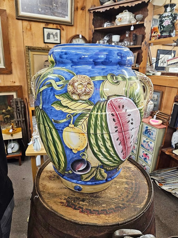 Admire the vibrant fruit designs on this large ceramic jar as it rests atop a rustic barrel for your viewing.