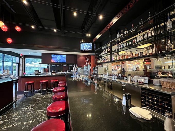 The bar gleams with promise, red stools standing ready for patrons seeking liquid comfort. Where strangers become friends over properly made Old Fashioneds.